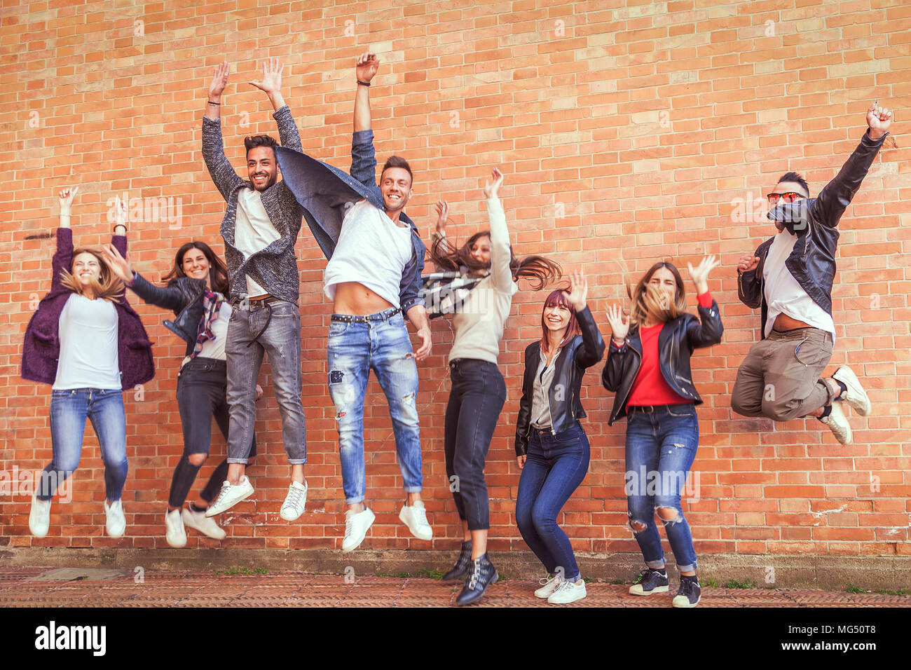large group of friends jumping together to have fun in front of a brick ...