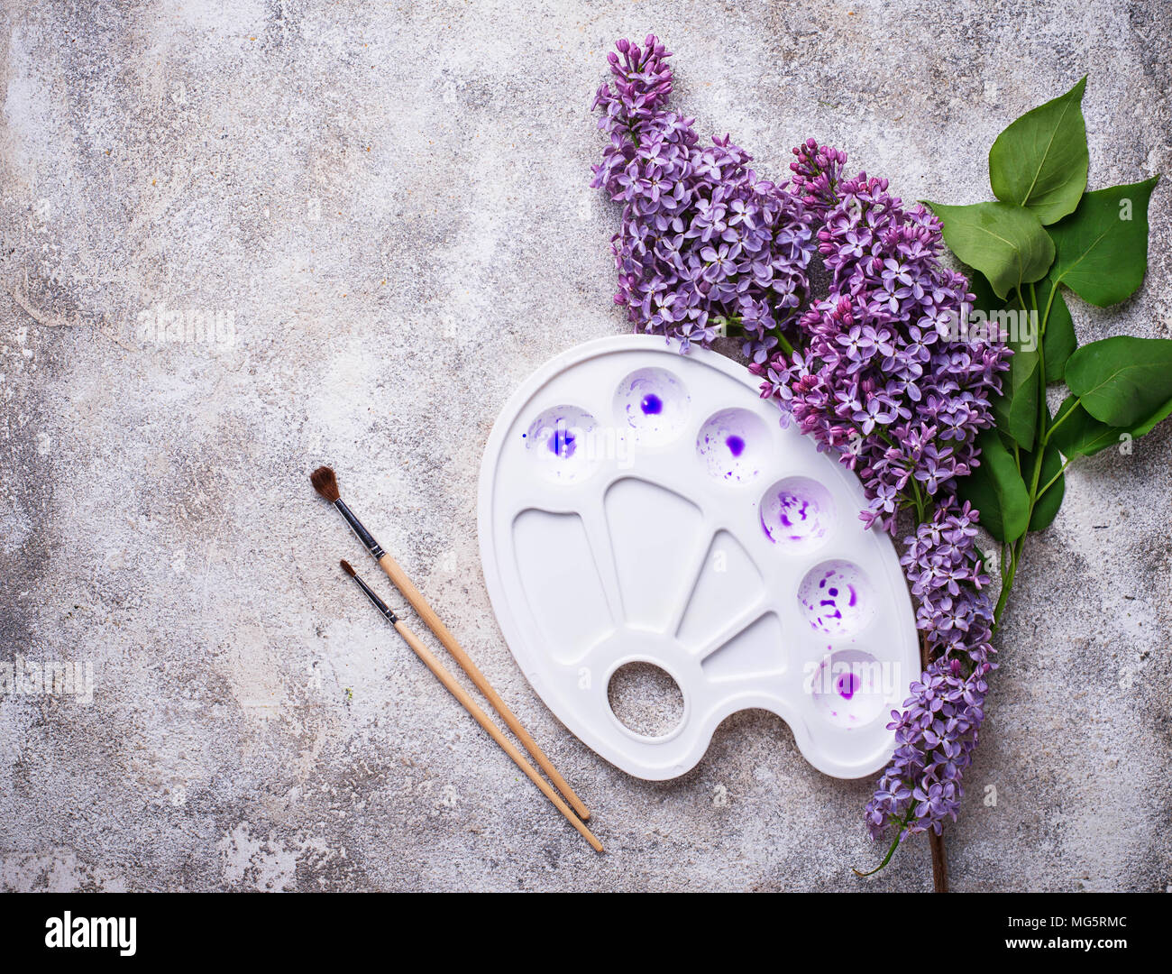 Artists palette with purple and violet paint and brushes on pink ...
