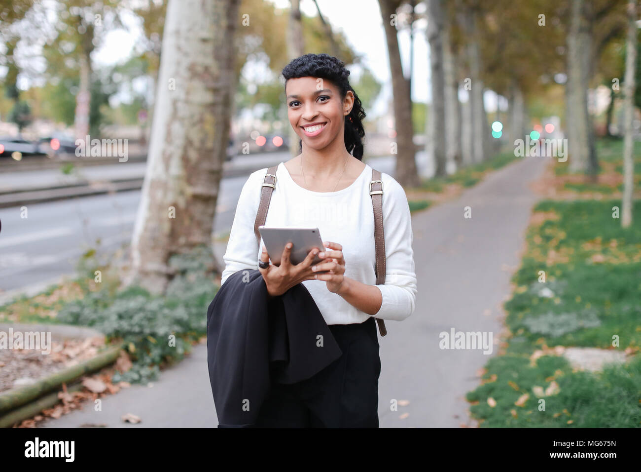Black smiling student walking with tablet near street with trees Stock ...