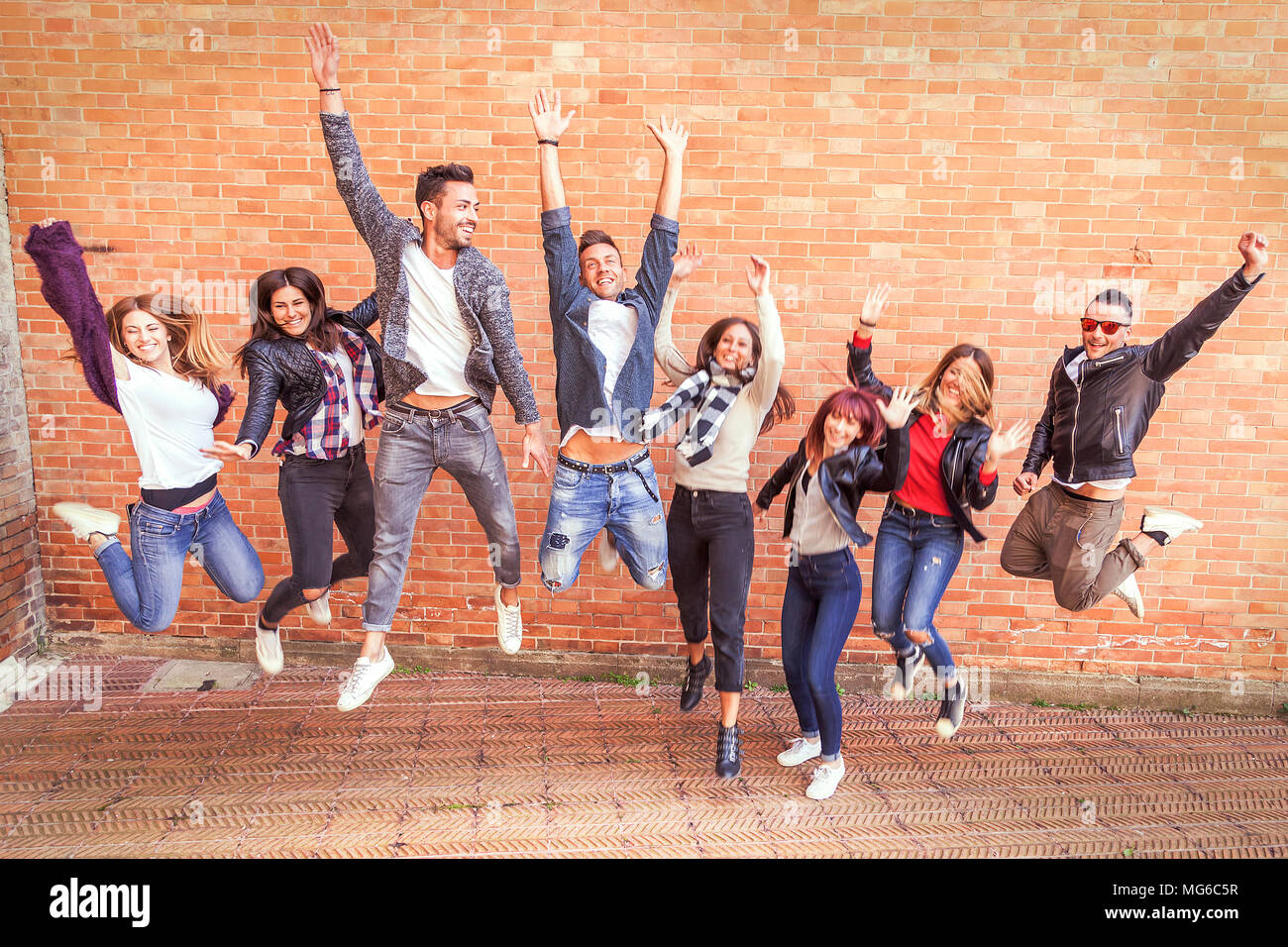large group of friends jumping together to have fun in front of a brick ...