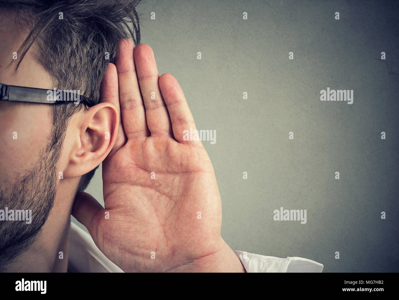 man holds his hand near ear and listens carefully isolated on gray wall ...