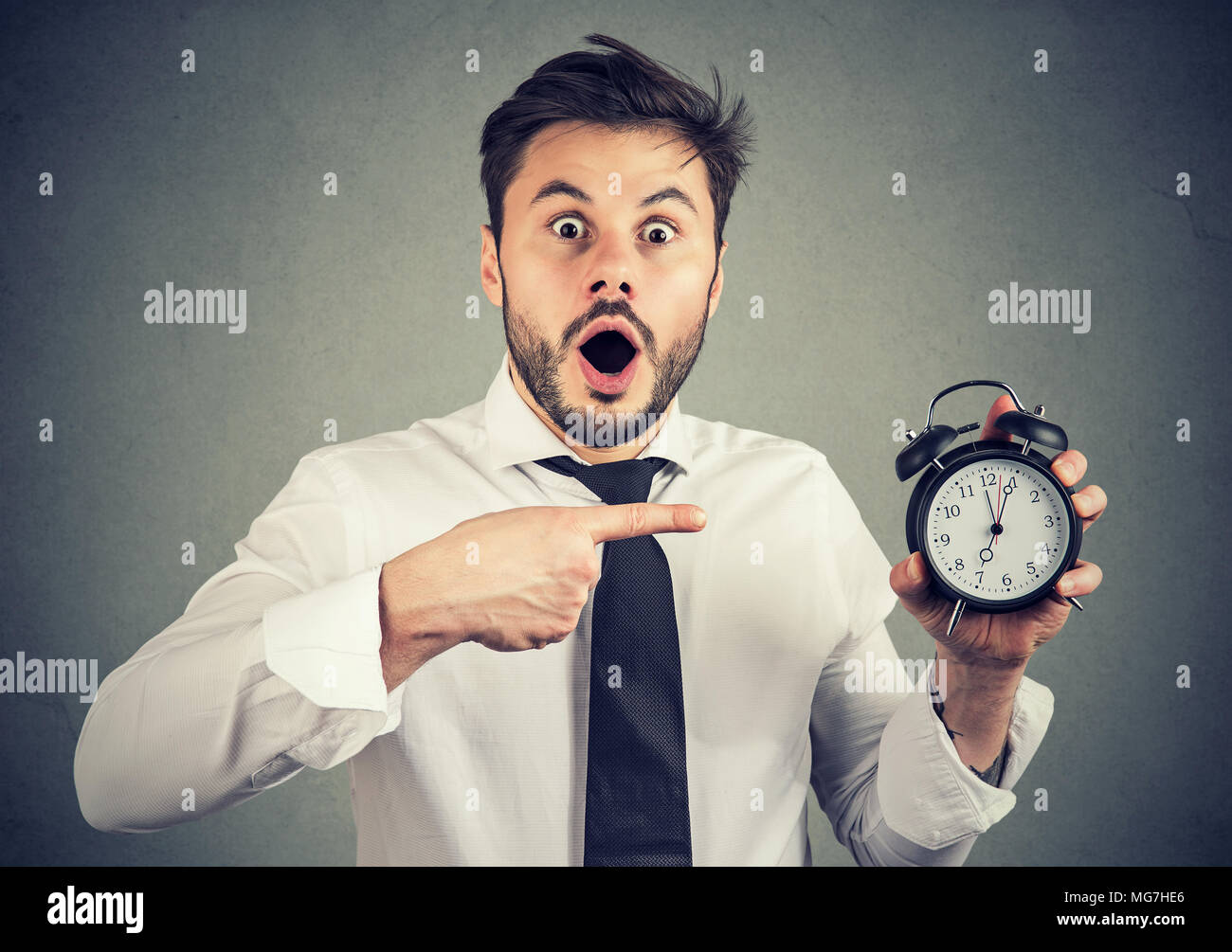 Expressive man in formal outfit holding alarm clock and pointing at it ...