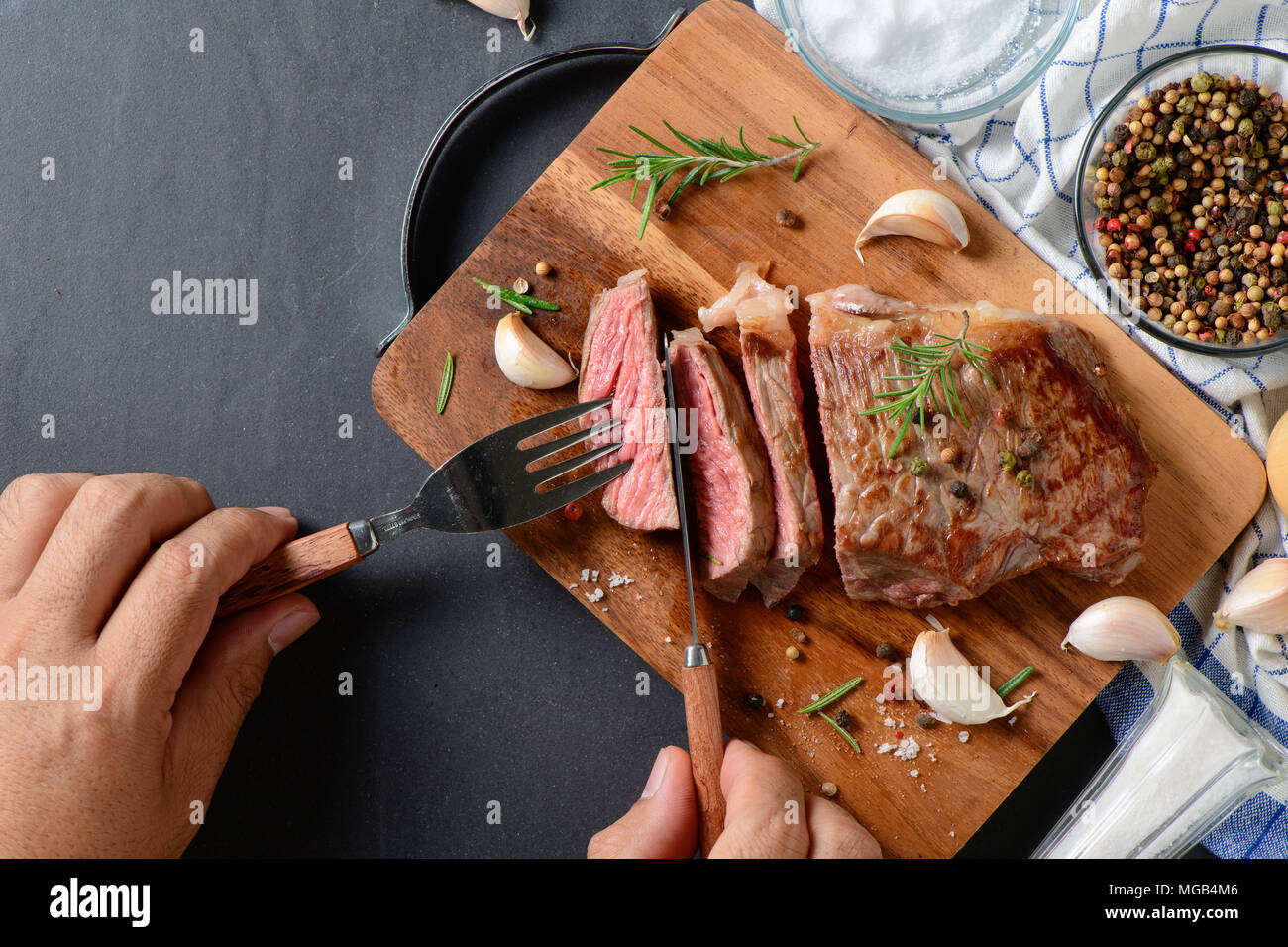 Man hand cutting beef steak with salt, garlic and rosemary leaf on ...