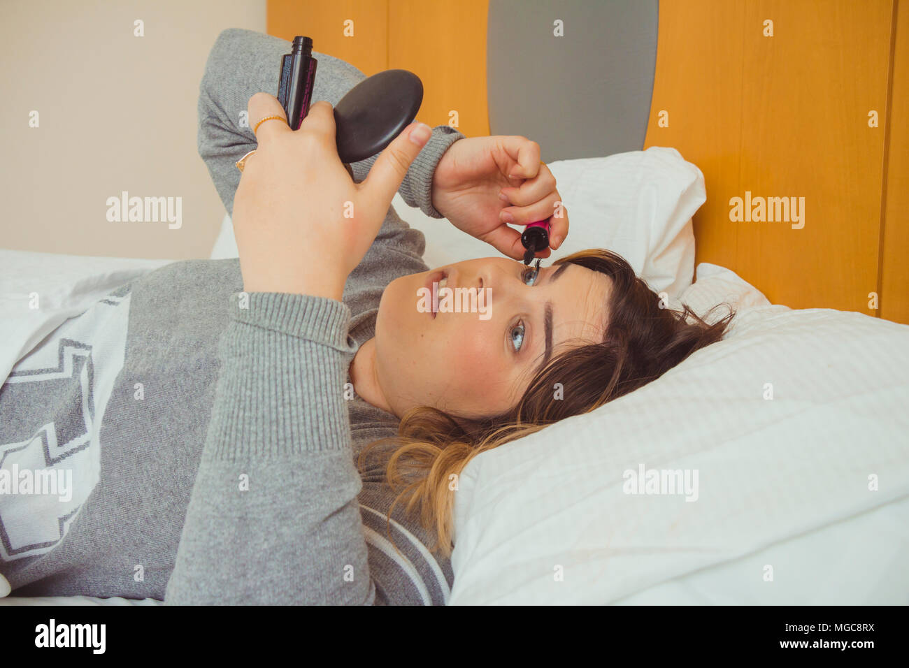 Woman applying makeup while she is lying on her bed Stock Photo - Alamy