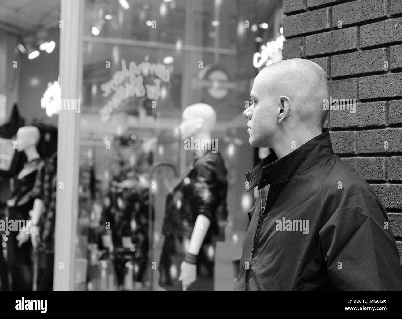Man with shaved head looking into shop window at mannequins, black and ...