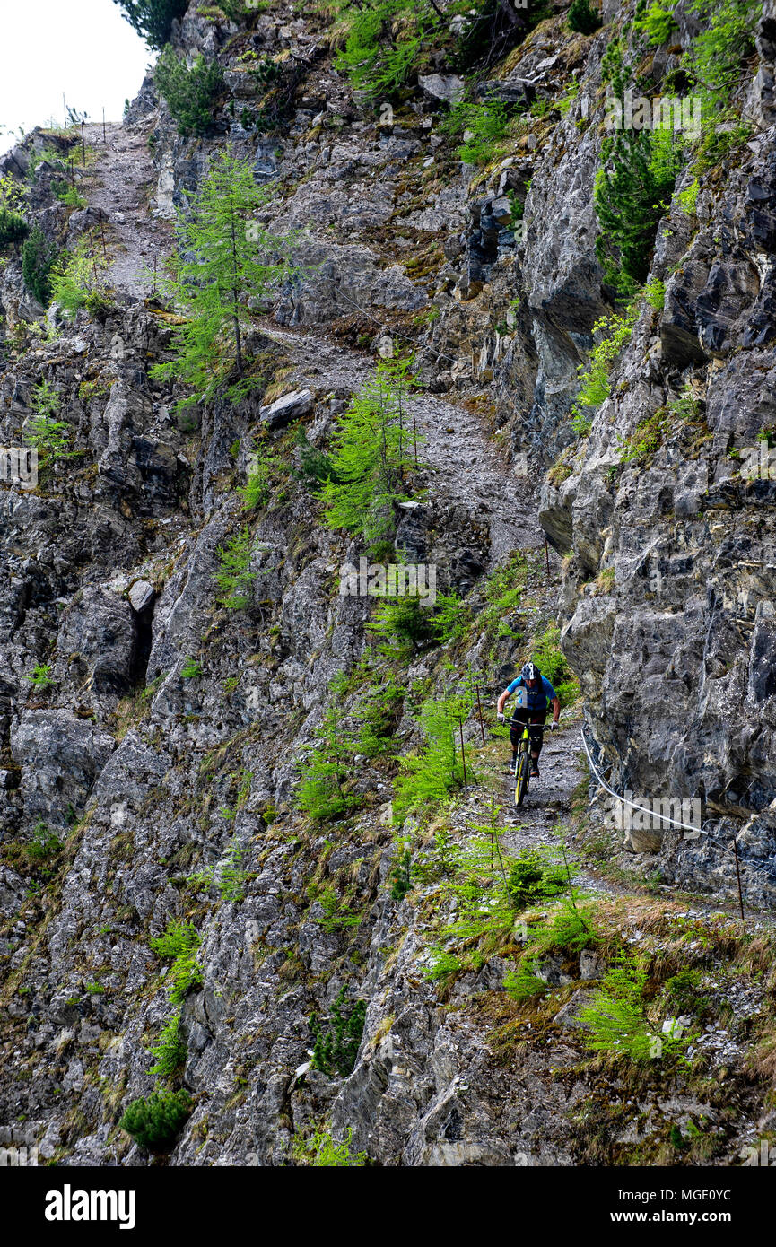 A man rides a mountain bike down a steep trail on the edge of a cliff ...