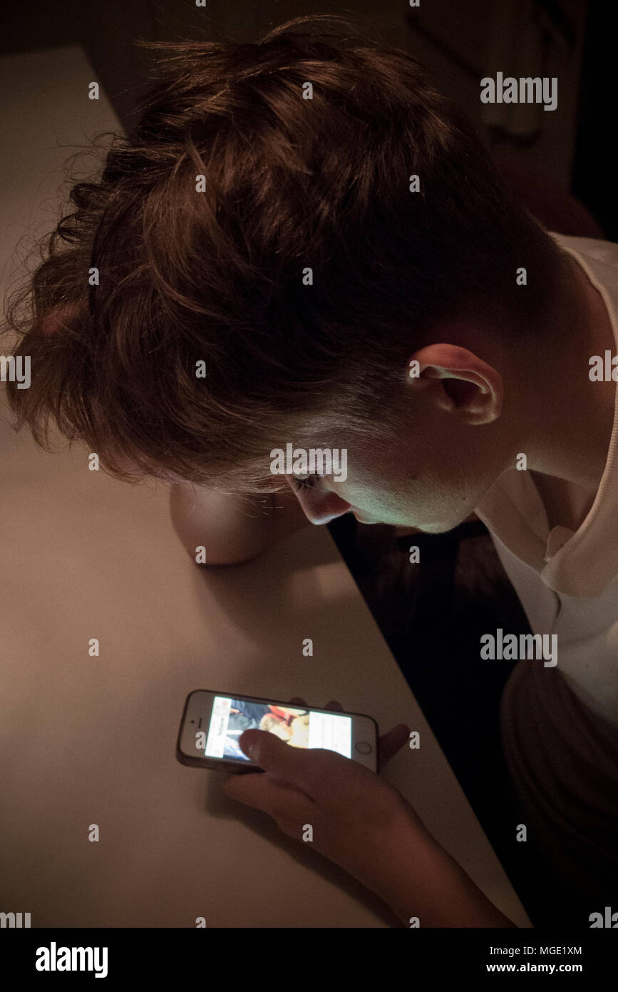 A teenager looks at his mobile phone in a dark room, the light ...