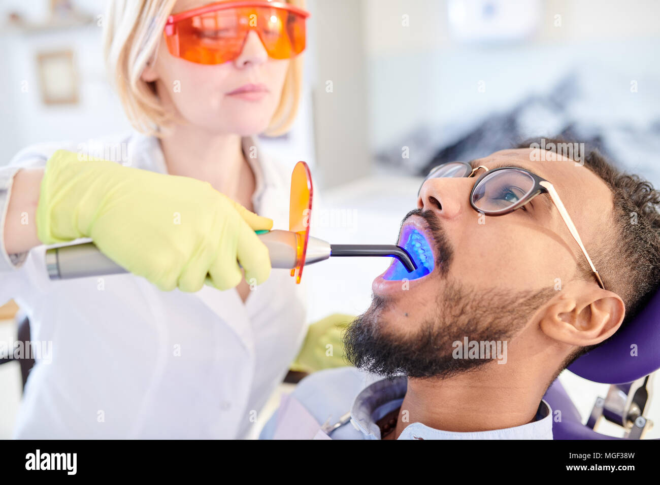 Bearded mixed-race patient sitting on dental chair with opened mouth ...