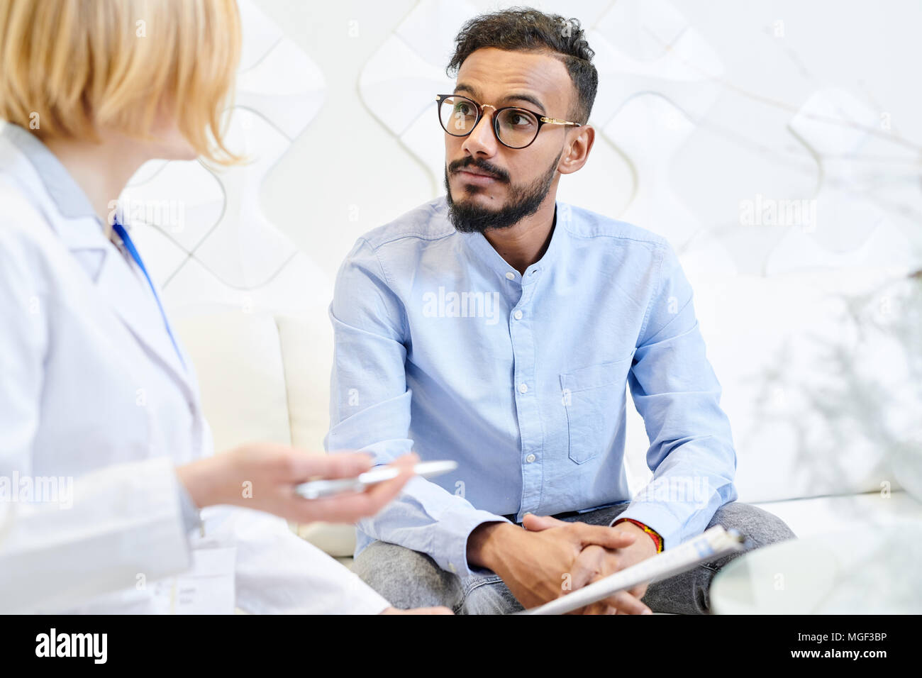 Portrait shot of mixed-race bearded patient sitting on cozy sofa and ...