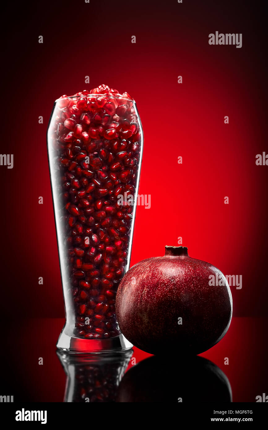 Pomegranate and glass filled with pomegranate seed on a reflective ...
