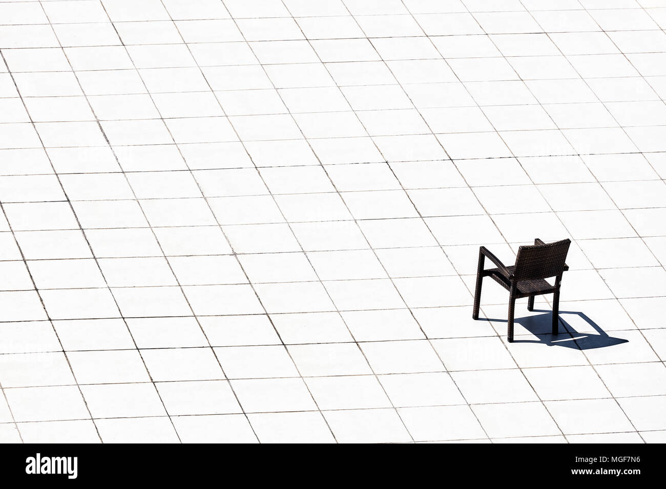 Single chair and its shadow on a wide space covered with white tile ...