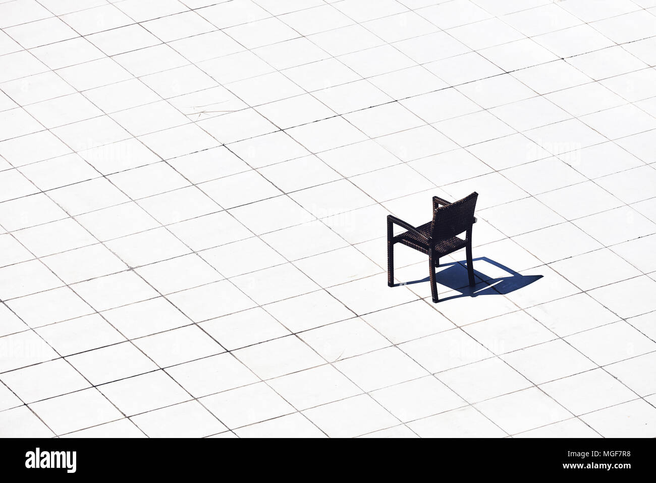 A minimalist view of a single chair and its shadow under the harsh sun ...