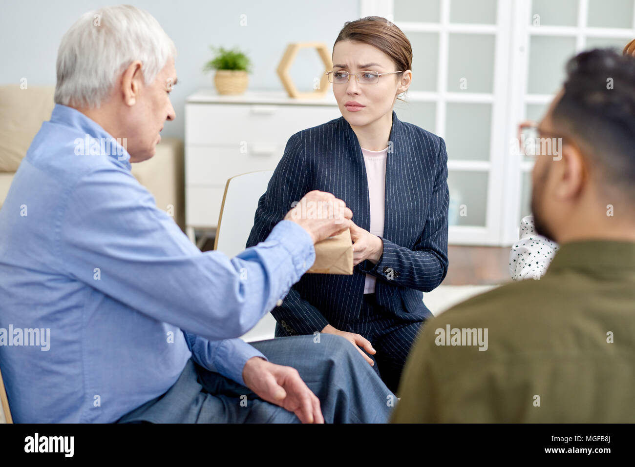 Friendly young psychiatrist passing paper tissue box to sad senior ...