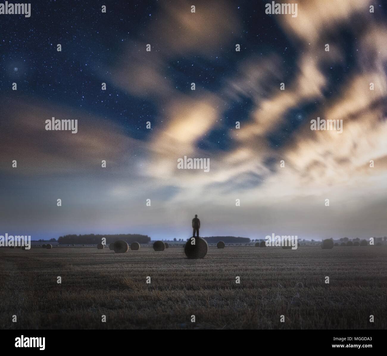 Strange man standing on field on straw bale under starry sky. Fine art ...