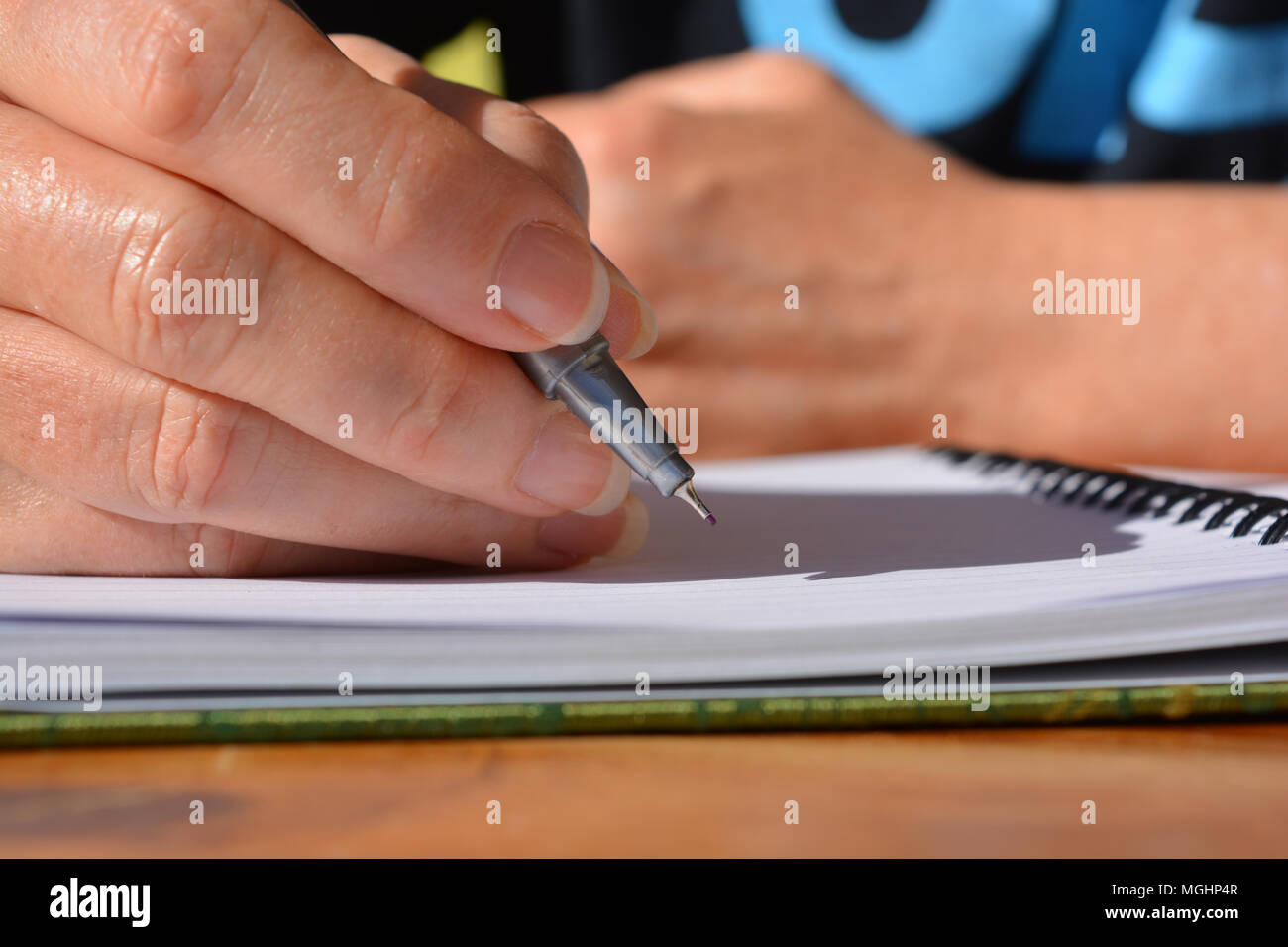 Woman with pen in hand, poised to write in a spiral bound notebook ...