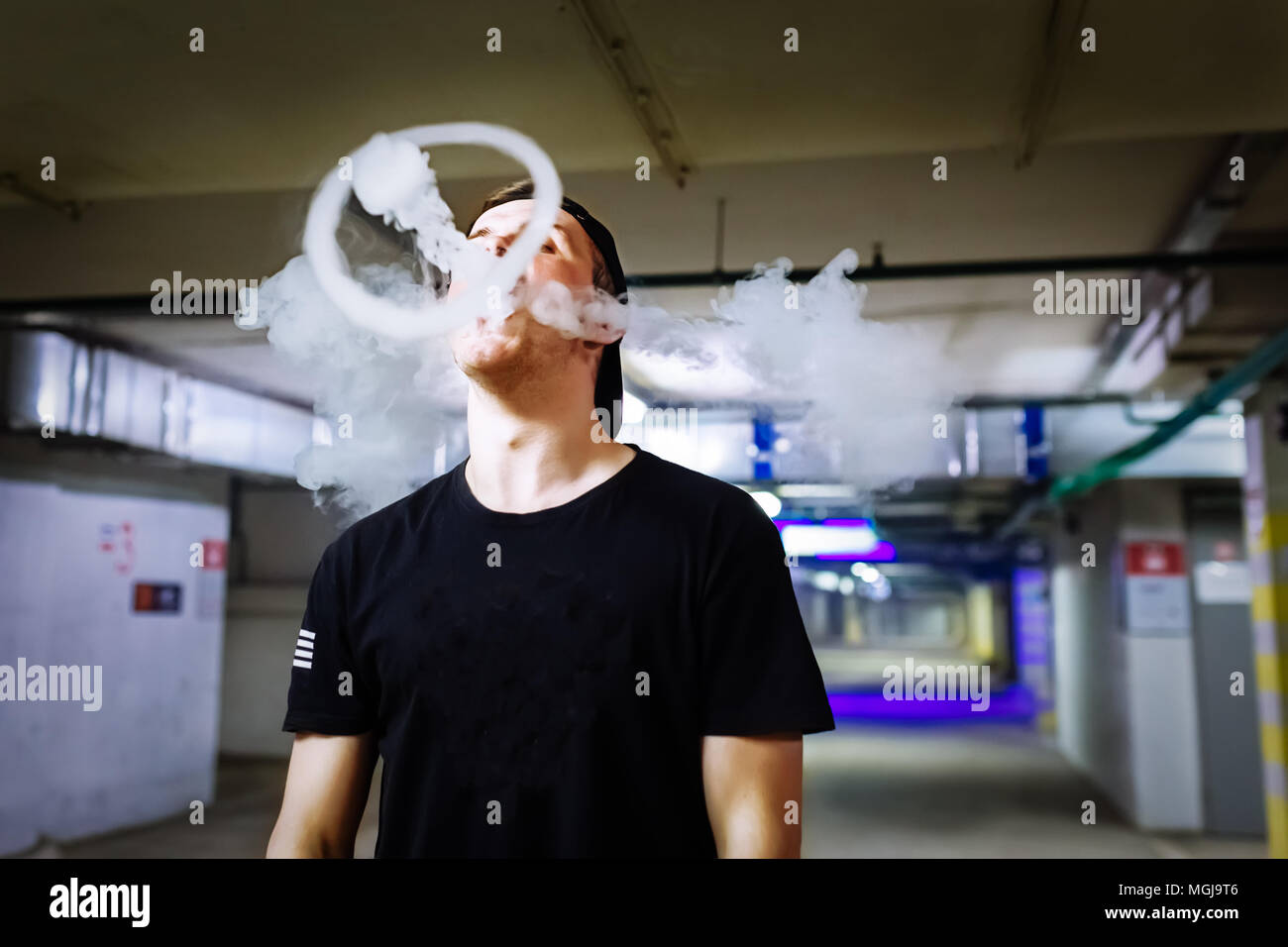 Man in cap smoke an electronic cigarette and releases clouds of vapor ...
