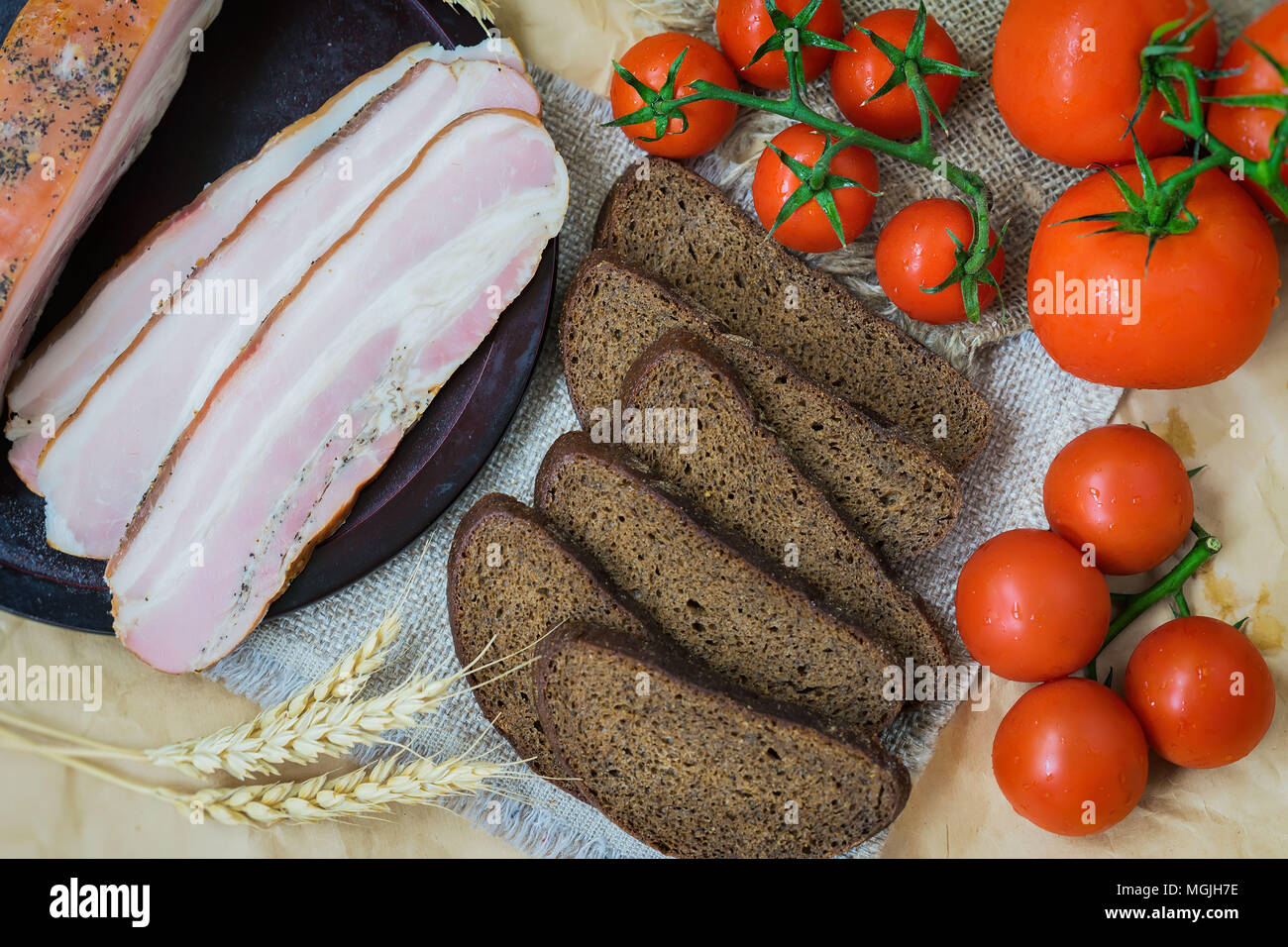 Close-up view of slices of pink bacon, pieces of rye bread, ripe red ...