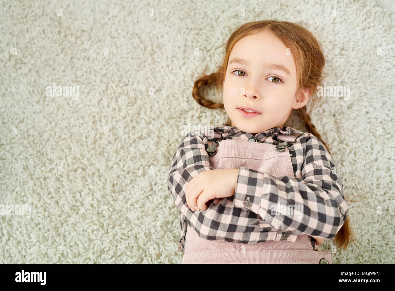 Waist-up portrait of cute little girl with two braids lying on cozy ...