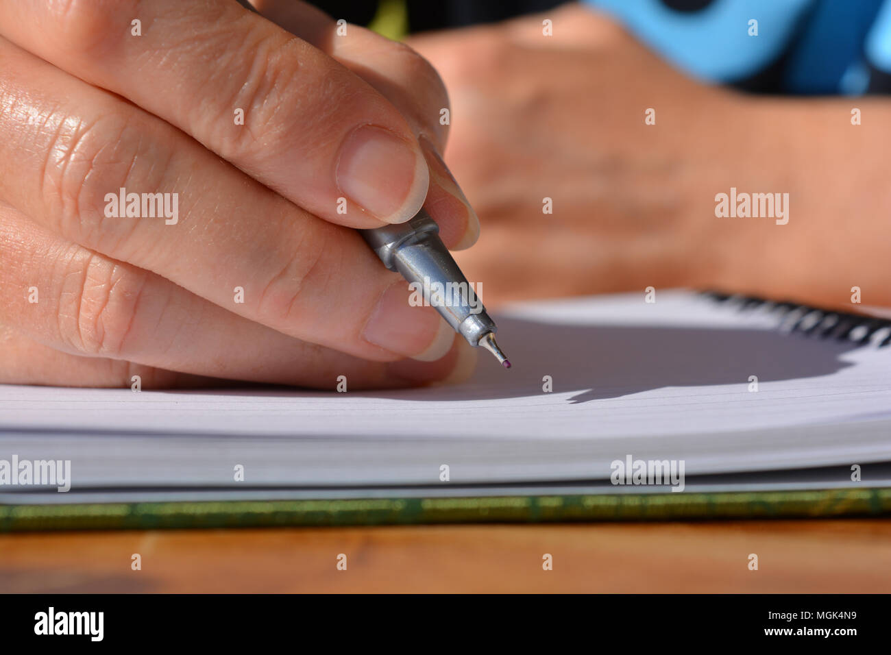 Woman with pen in hand, poised to write in a spiral bound notebook ...