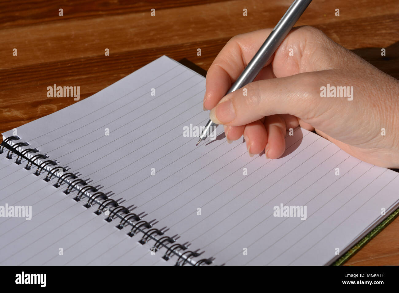 Woman with pen in hand, poised to write in a spiral bound notebook ...