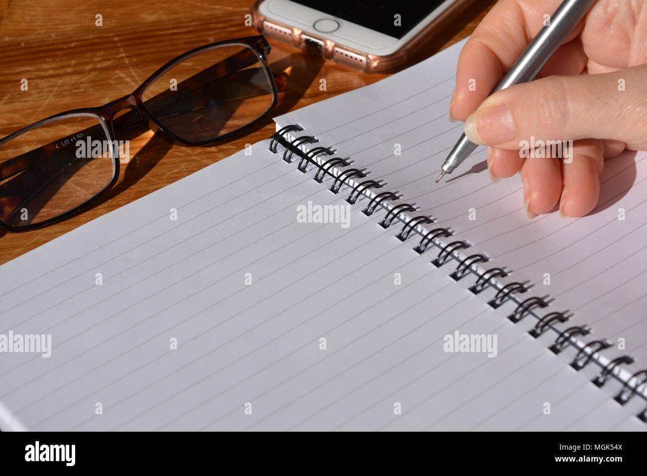 Woman with pen in hand, poised to write in a spiral bound notebook ...