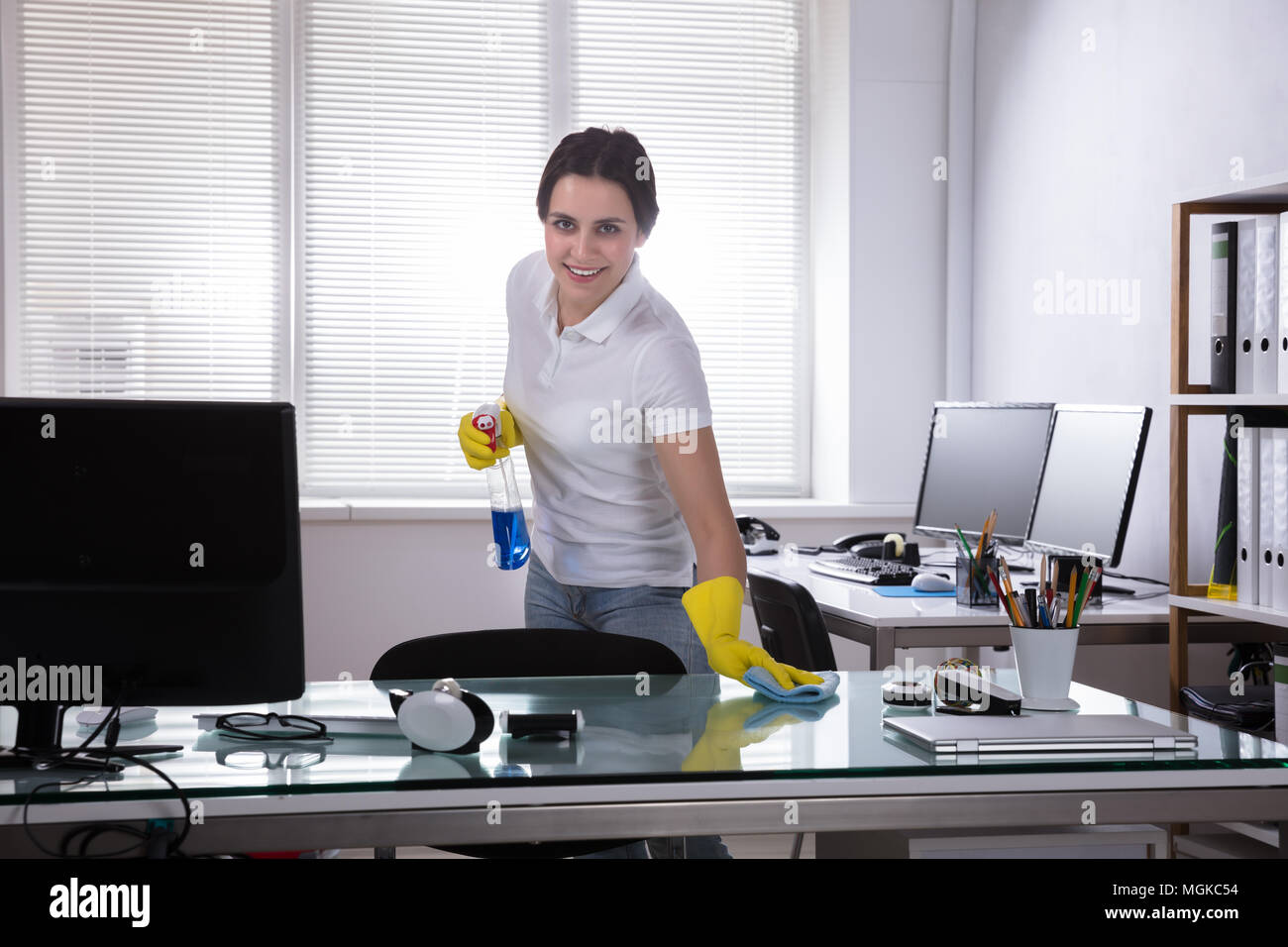 Smiling Female Janitor Cleaning Desk With Rag In Office Stock Photo - Alamy