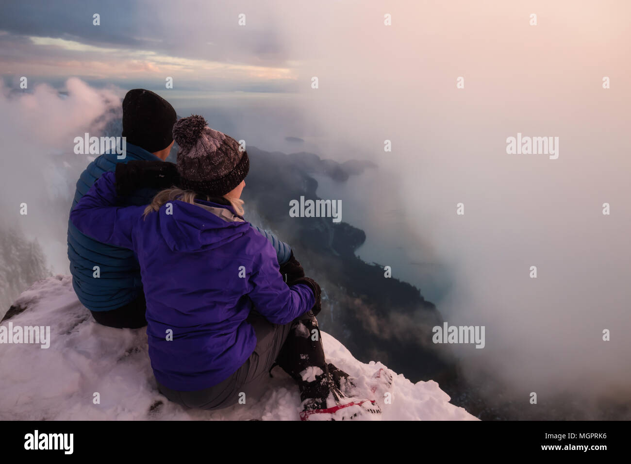 Young couple sitting on the side of a steep cliff overlooking the ...