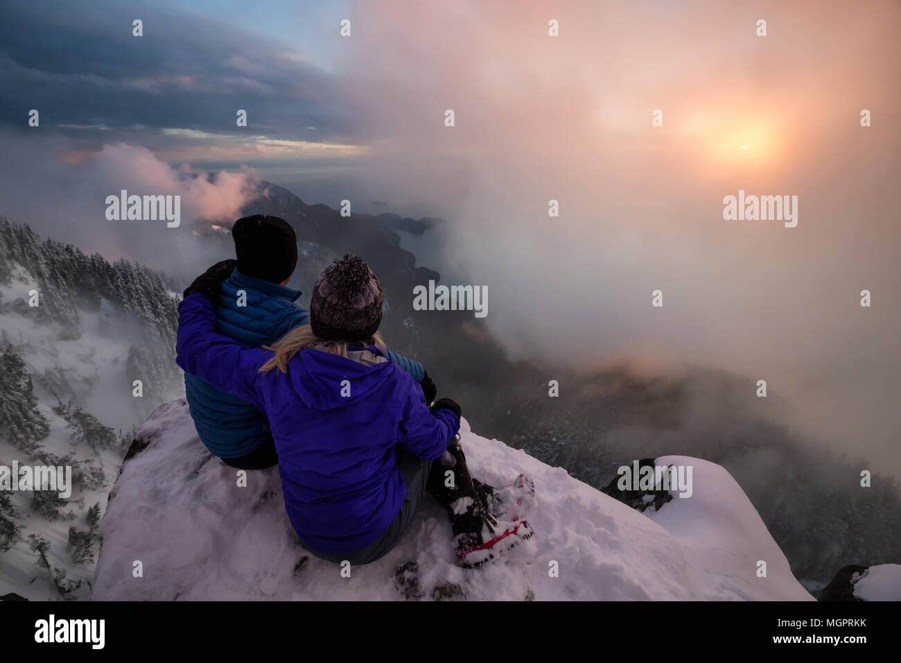 Young couple sitting on the side of a steep cliff overlooking the ...