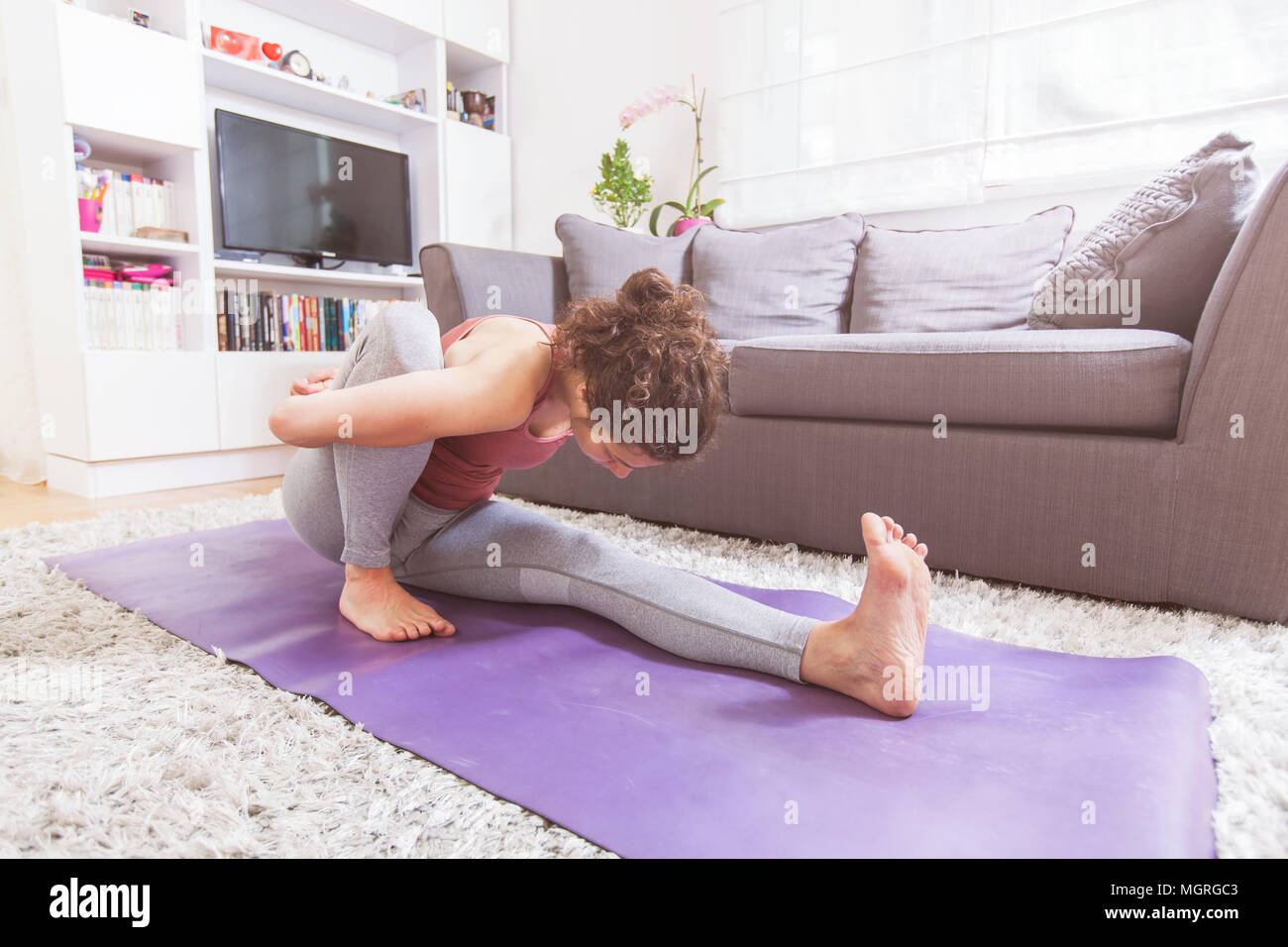 Woman doing Yoga exercise at Home, variation of janu sirsasana pose ...