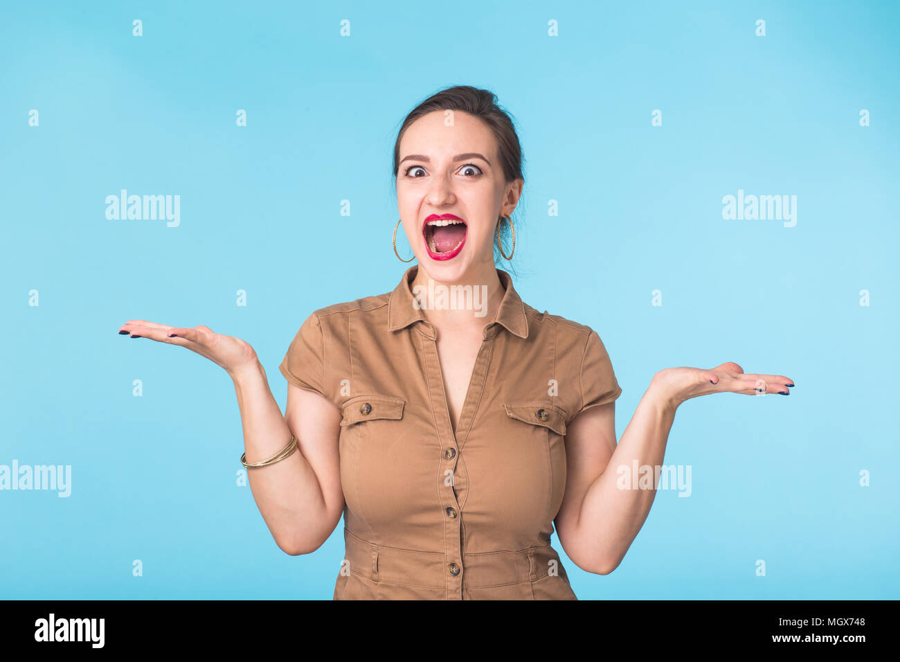 Surprised young woman shouting over blue background. Looking at camera ...
