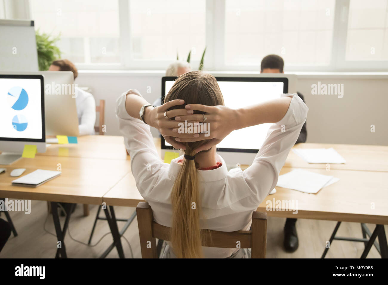 Woman relaxing at workplace holding hands behind head, back view Stock ...