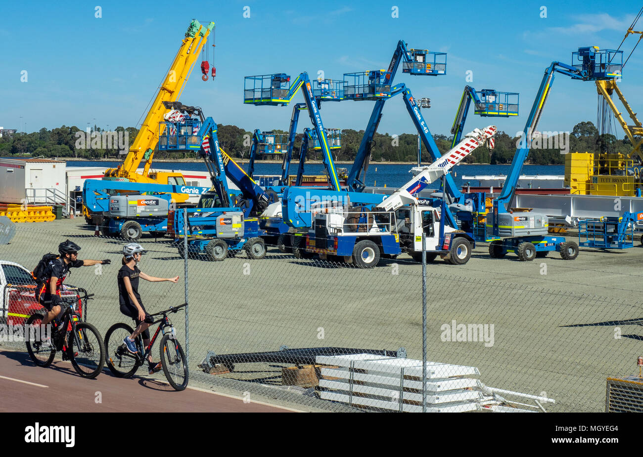 Two cyclists looking into a worksite full of cherry pickers, or aerial ...