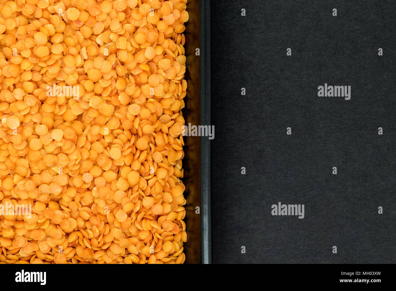 Red lentil grains in black plate on black stone background surface with ...