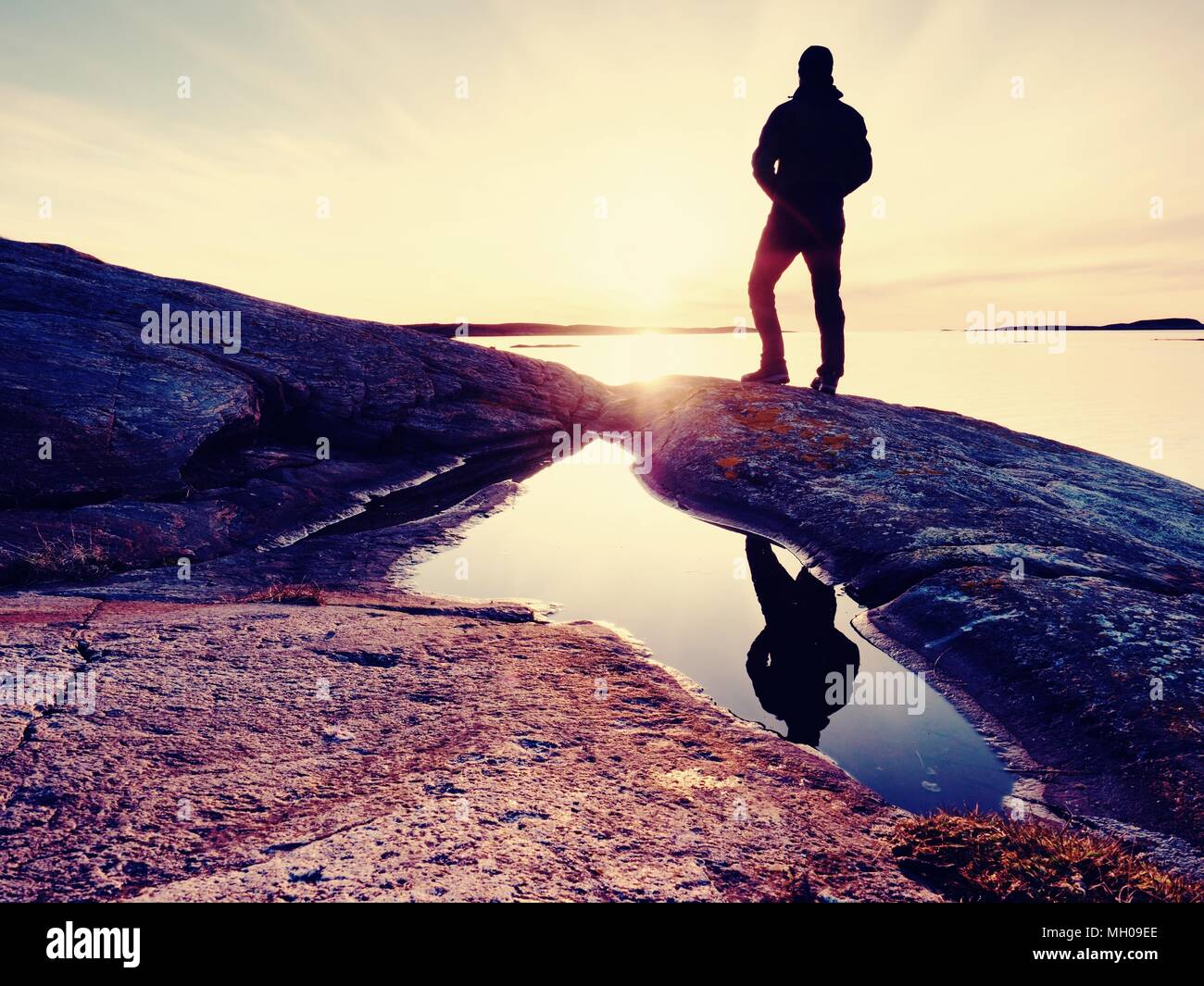 Silhouette of man in outdoor clothes on rocky cliff above sea ...