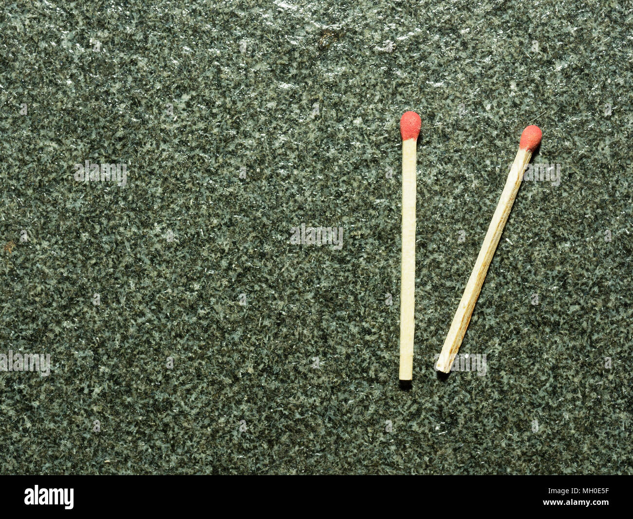 Two wooden match sticks with red head over black or dark granite ...