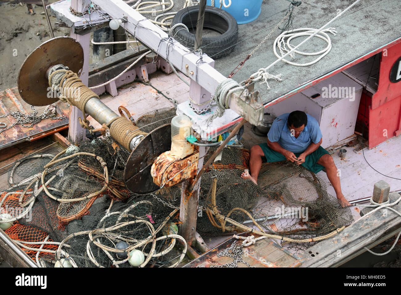 Fisherman using his down time when tide receded to repair his fishing ...