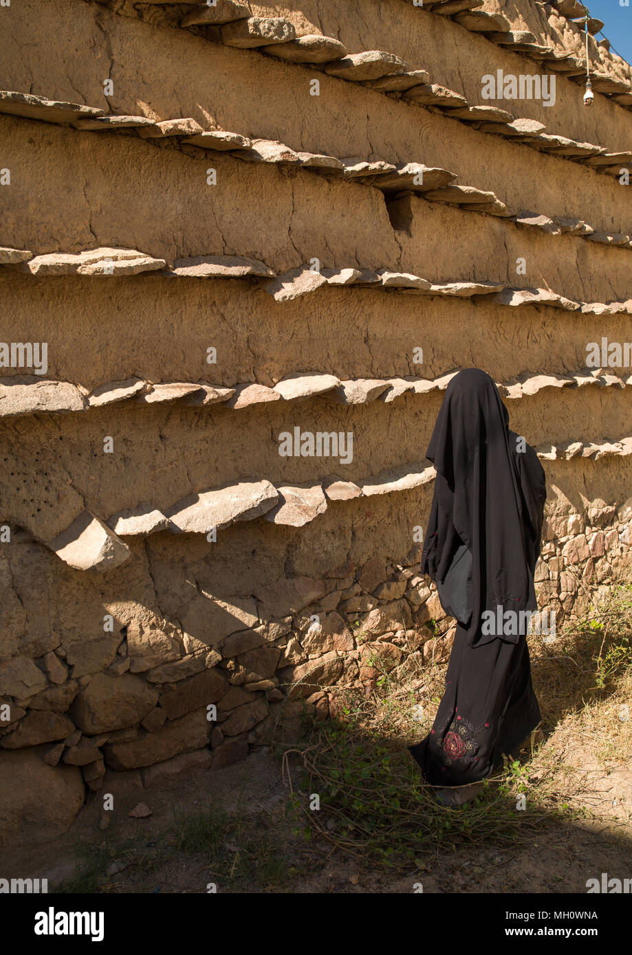 Saudi woman in front of traditional clay and silt homes in a village ...