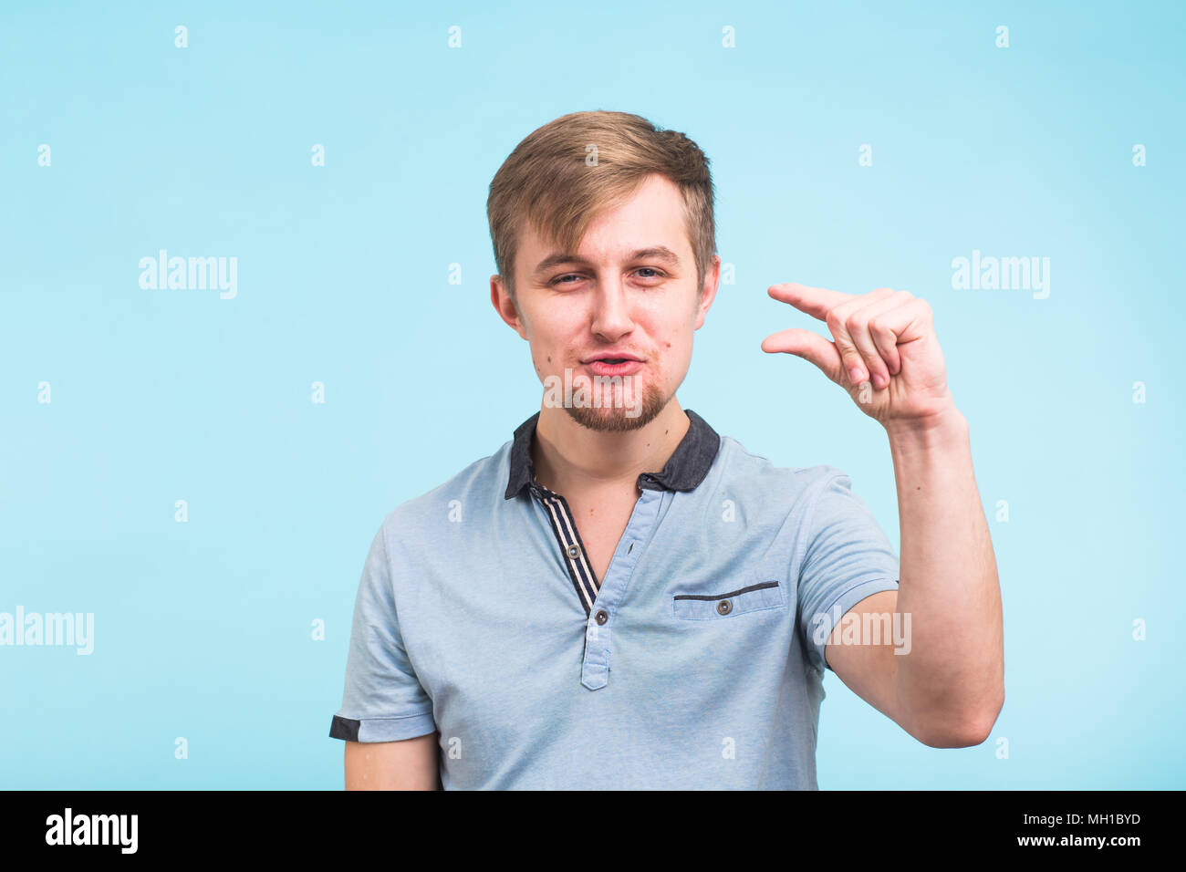 Positive handsome man shows something very tiny or small over blue ...