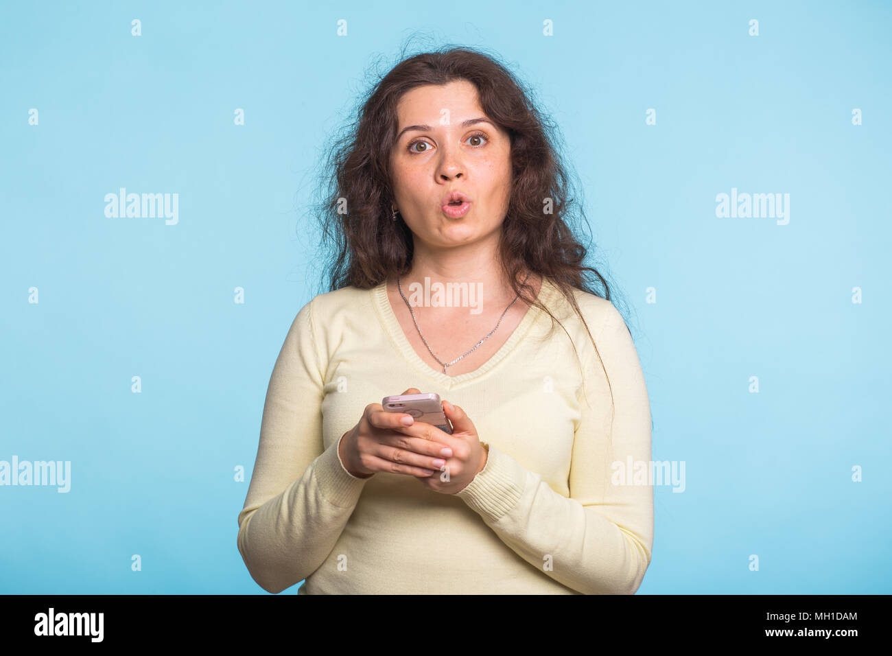 Portrait shocked young woman holding mobile phone isolated over blue ...