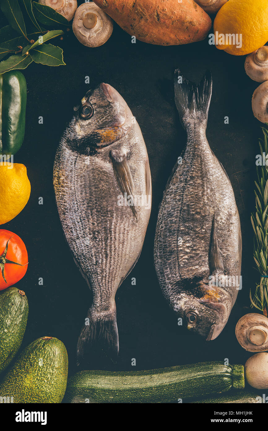 Top view of fish on rough board with spices and different vegetables ...