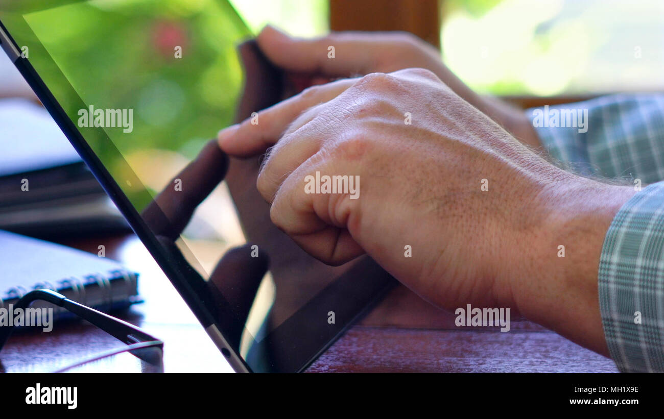 Man using tablet device closeup at desk, backlit by sunshine with ...