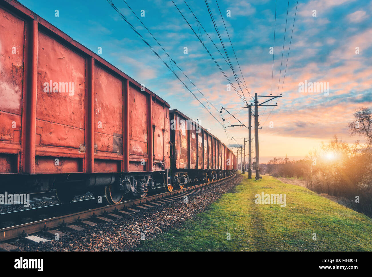 Red cargo wagons and train on railway station against blue sky with ...
