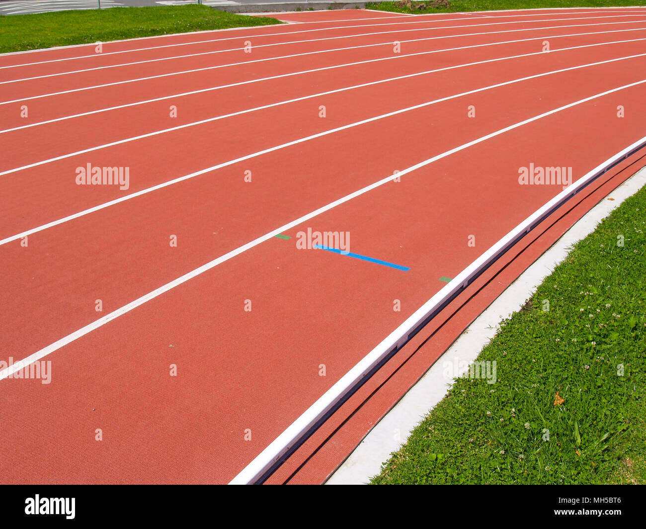 Bright red synthetic running track withe clear white lanes marked Stock ...