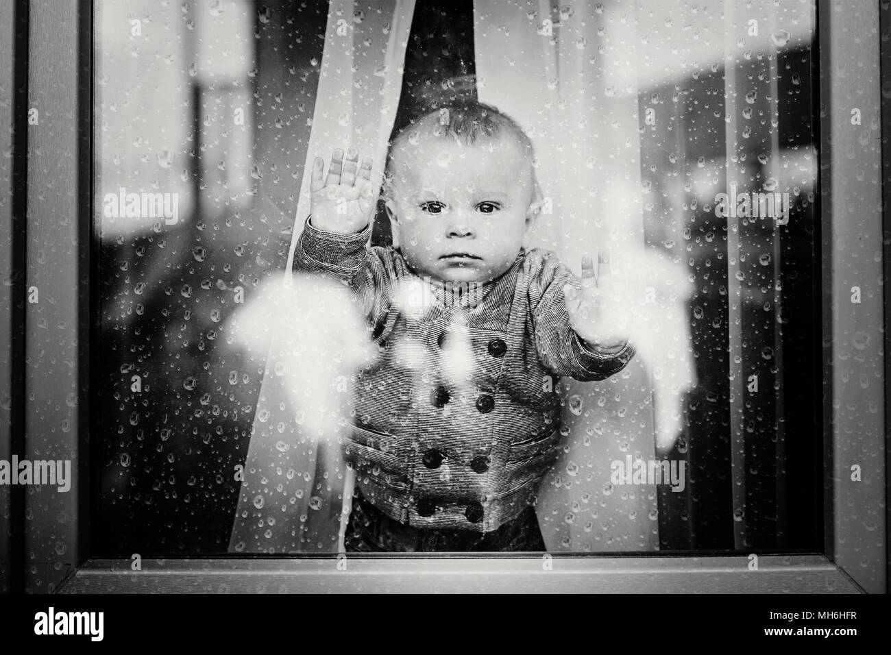 Cute toddler boy, staying at home behind the glass doors or window ...