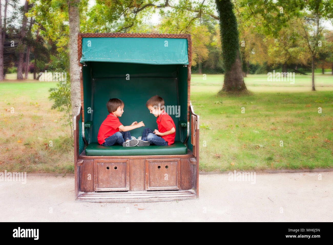 Two kids, brothers,sitting in a sheltered bench, playing hand clapping ...