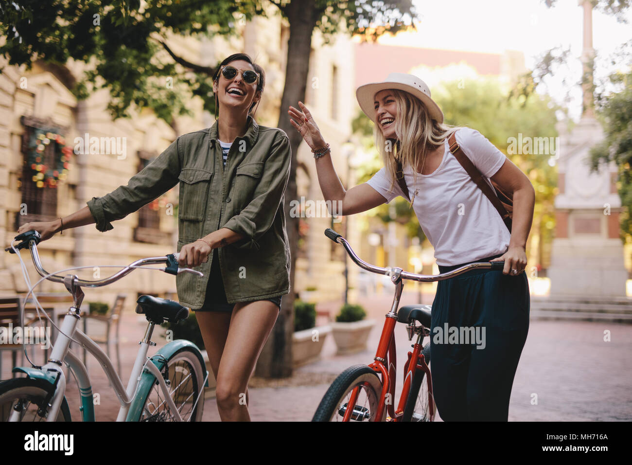 Positive and happy girls walking on the city street with bicycles ...