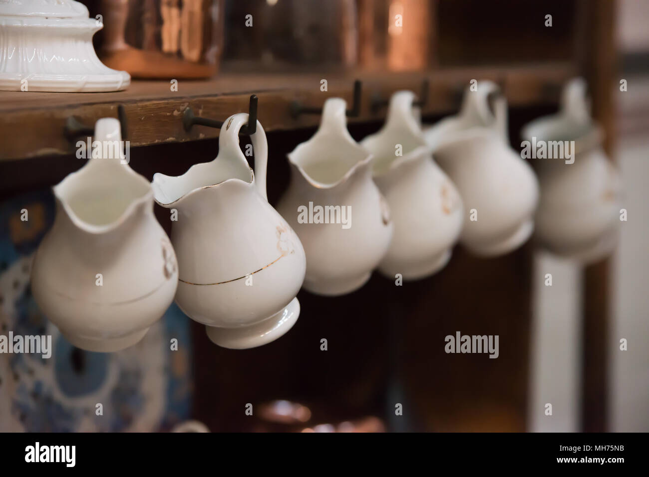 Old Victorian creamer jugs hanging od wooden rack in mansion kitchen ...