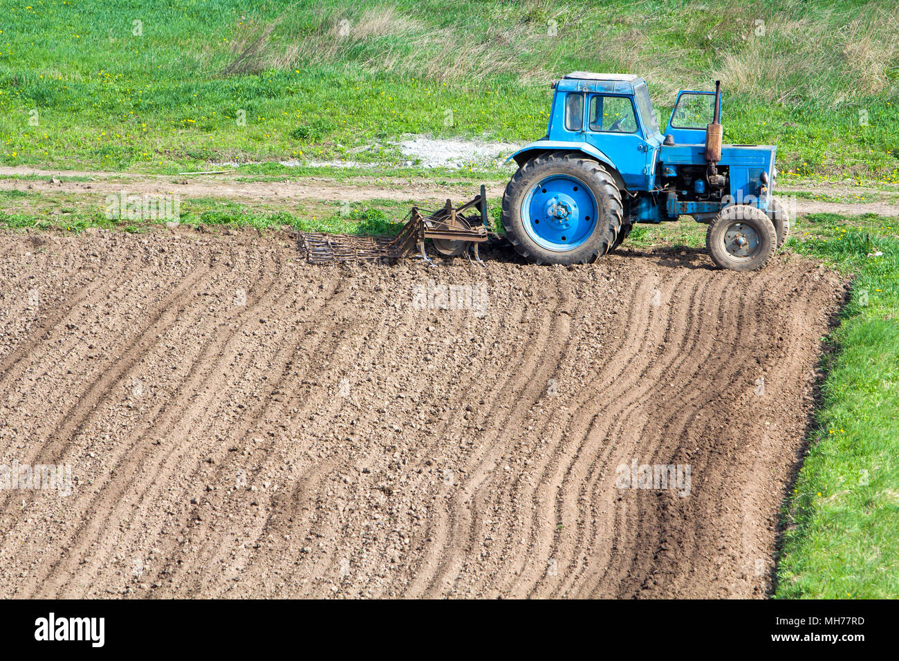 Blue dusty tractor with seedbed cultivator standing at the edge of ...