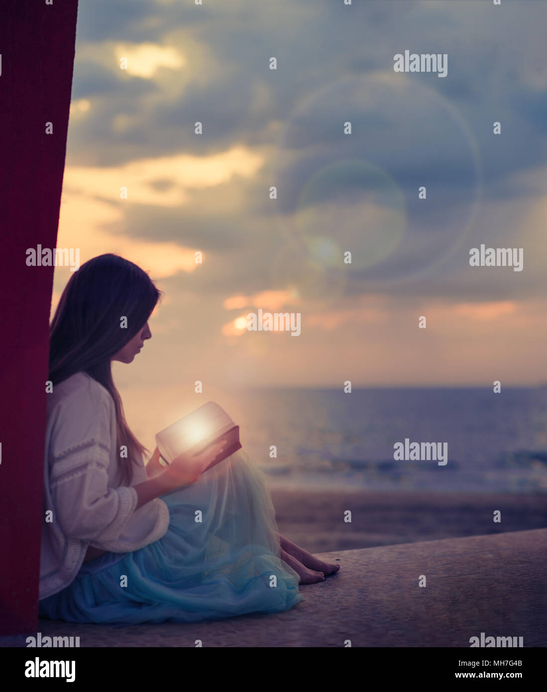 girl reading a magic book sitting at sea shore Stock Photo - Alamy