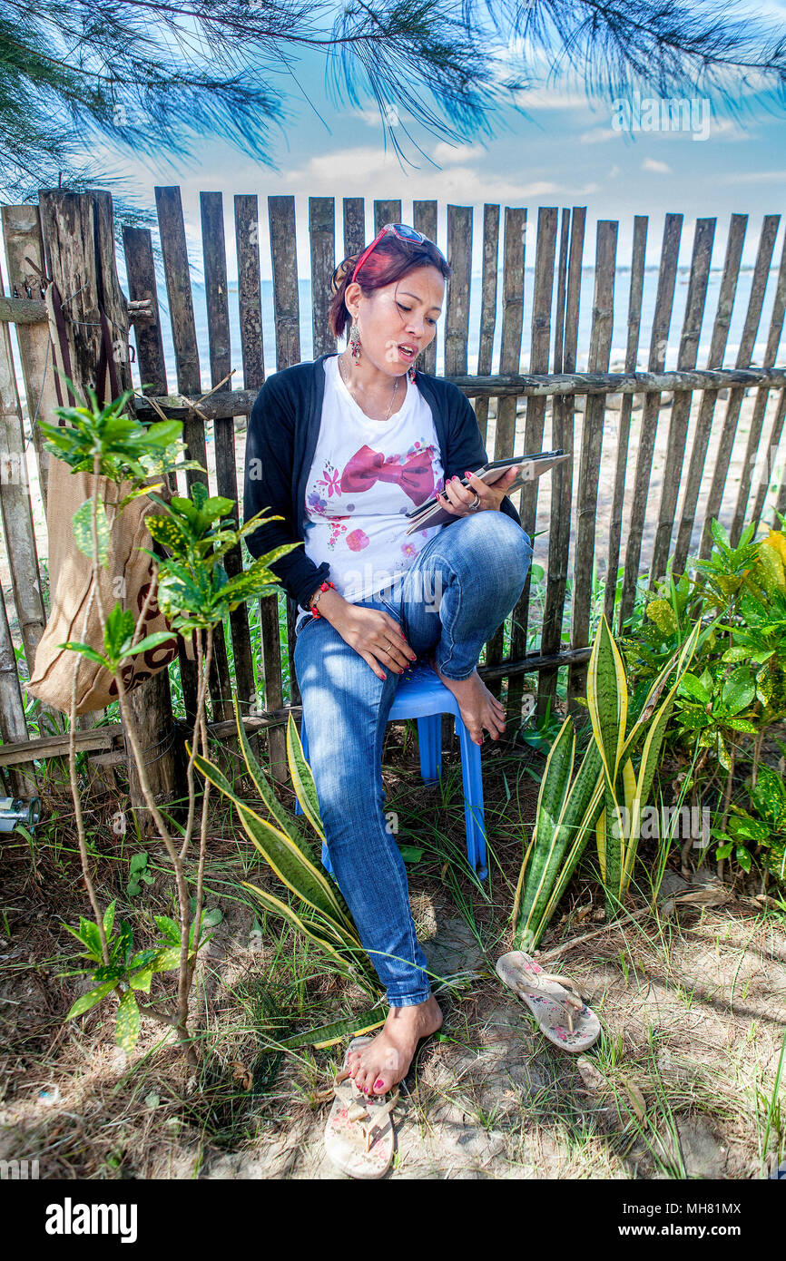 A Filipino woman sits at a beach resort having a voice call using her ...